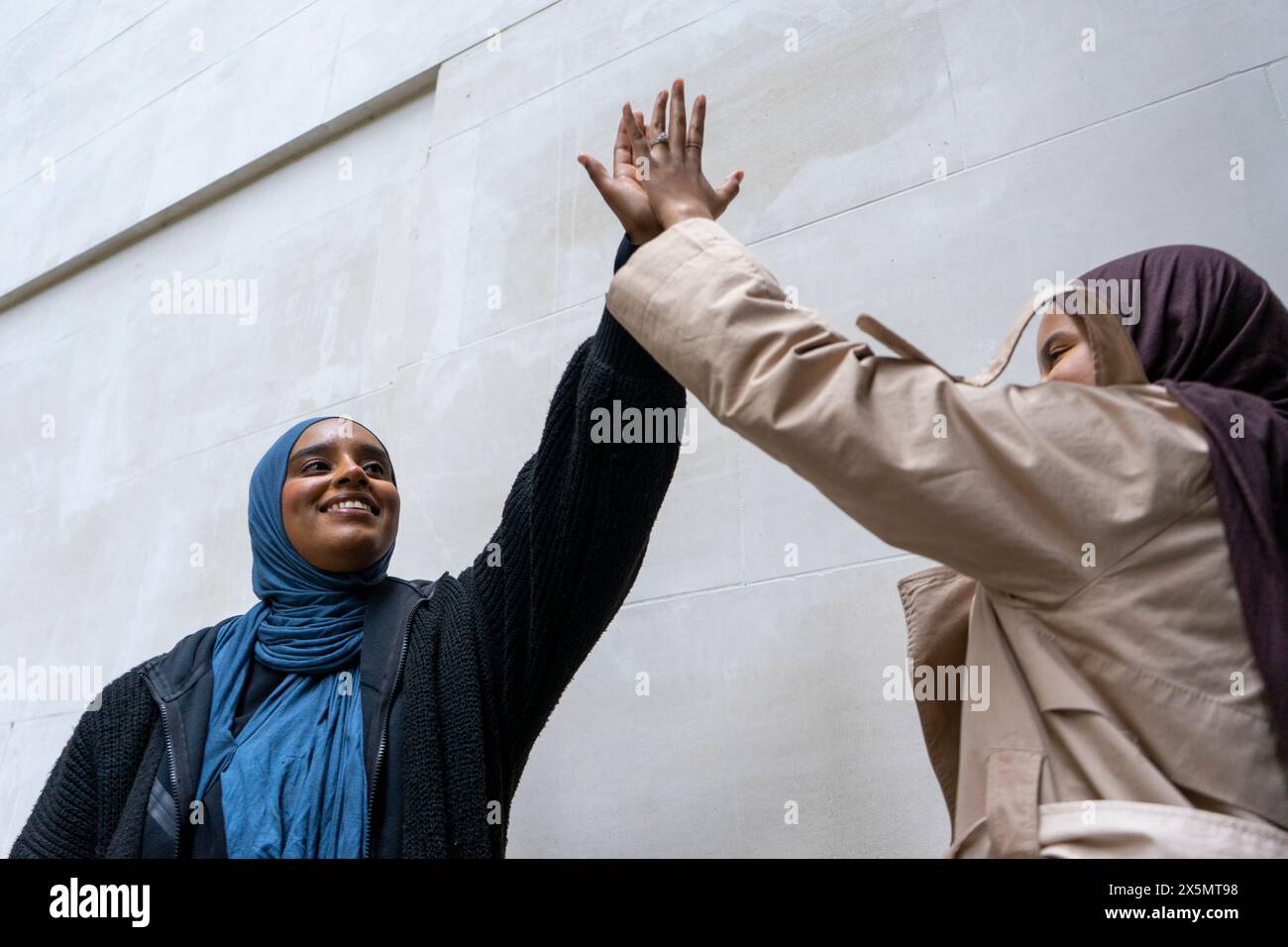 Two women wearing hijabs doing high-five Stock Photo - Alamy