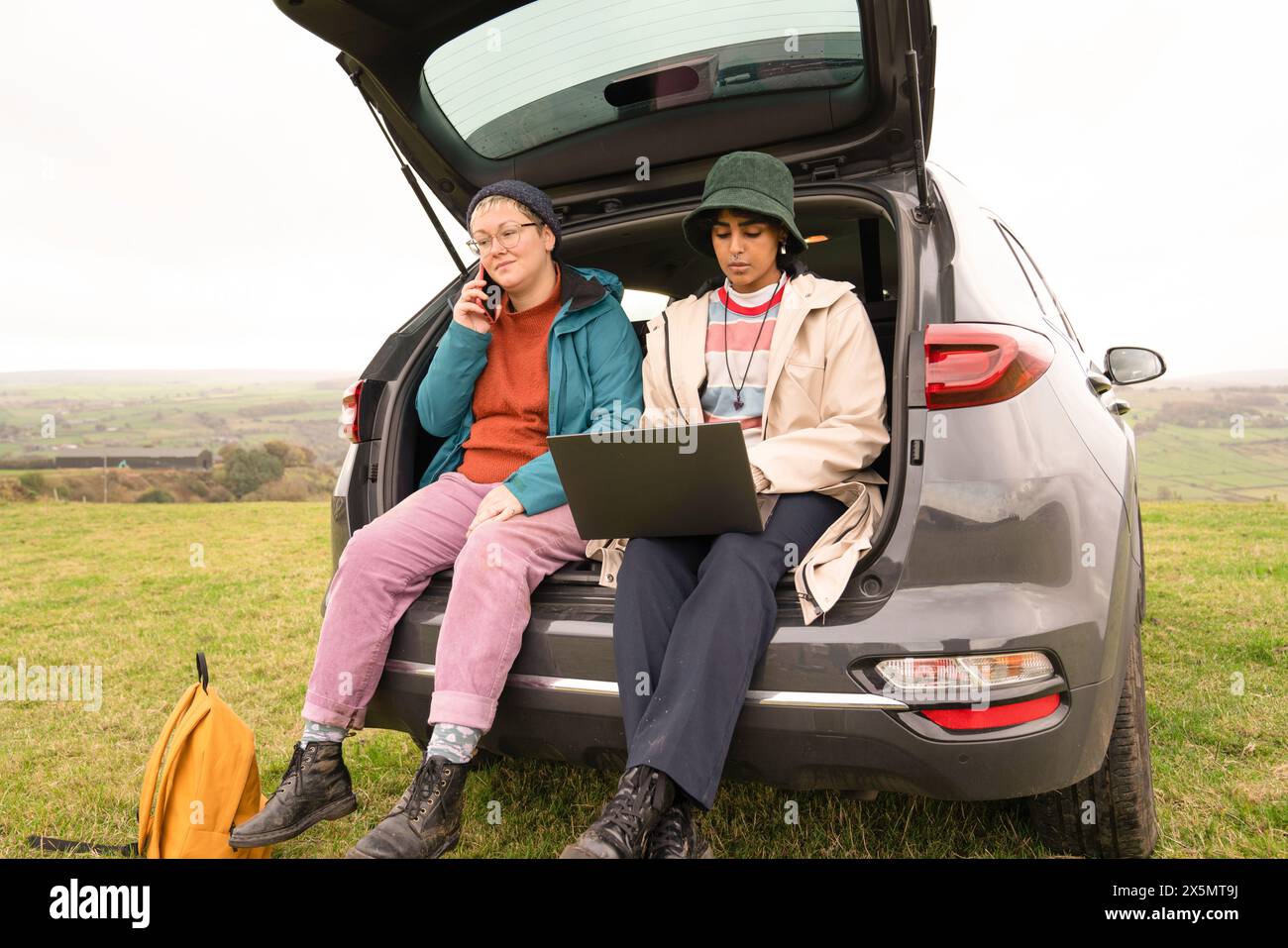 Female hikers sitting in car trunk and using phone and laptop Stock ...
