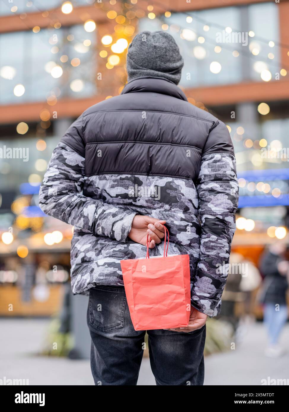 Man holding bag with Christmas present behind back Stock Photo - Alamy