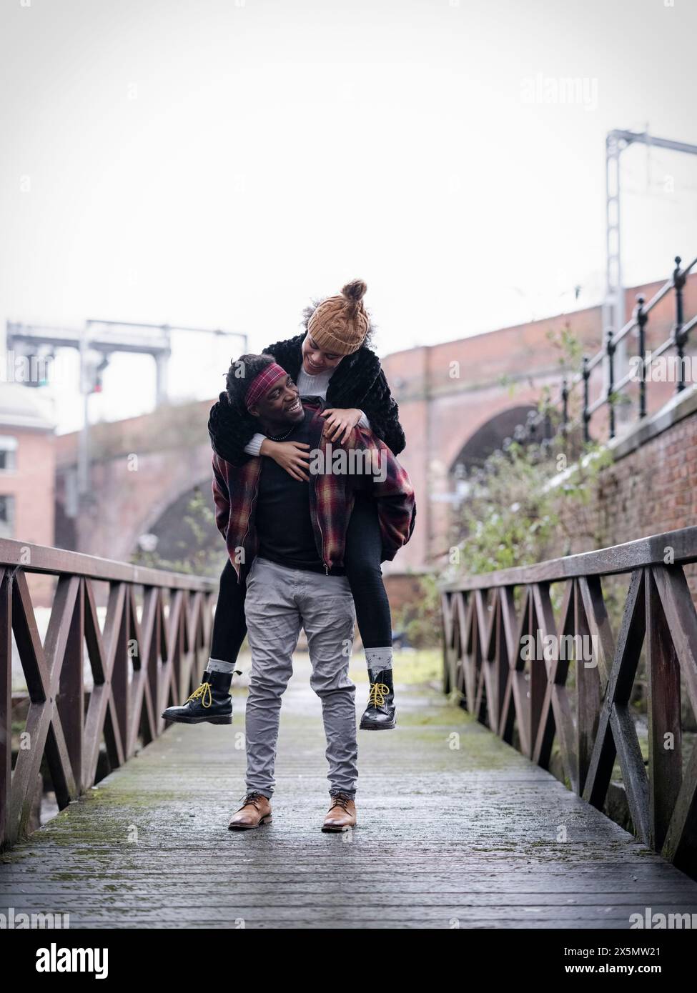 Smiling man carrying girlfriend on back on footbridge Stock Photo - Alamy