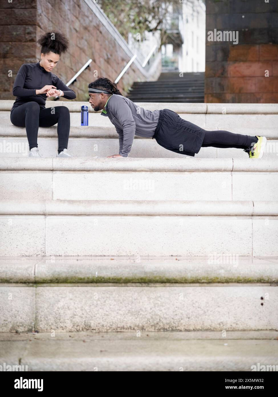 Athletic woman assisting man doing push-ups on steps outdoors Stock ...
