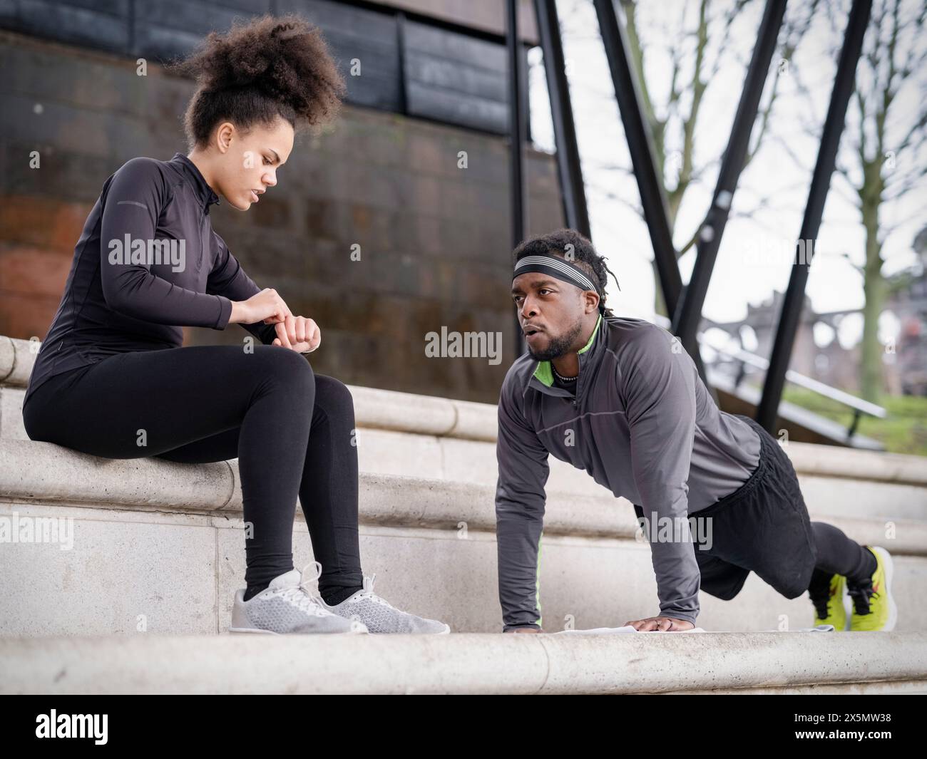 Athletic woman assisting man doing push-ups on steps outdoors Stock ...