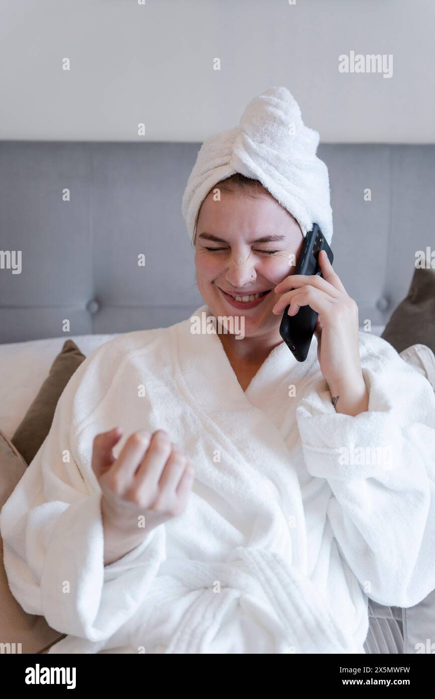 Woman in bathrobe and towel turban talking on smart phone on bed Stock ...