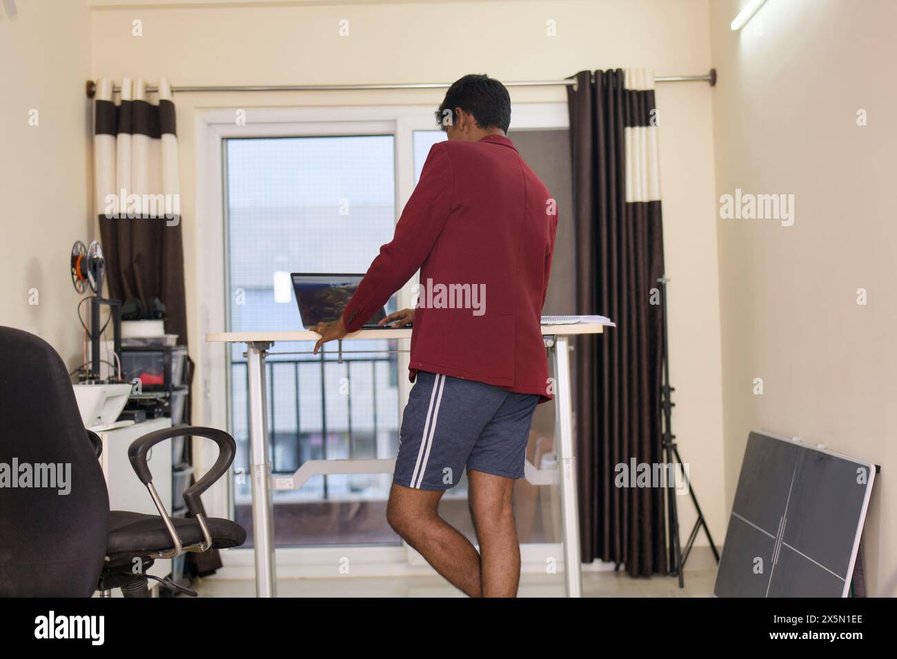 A young man stands at his home office desk, engrossed in work on his ...