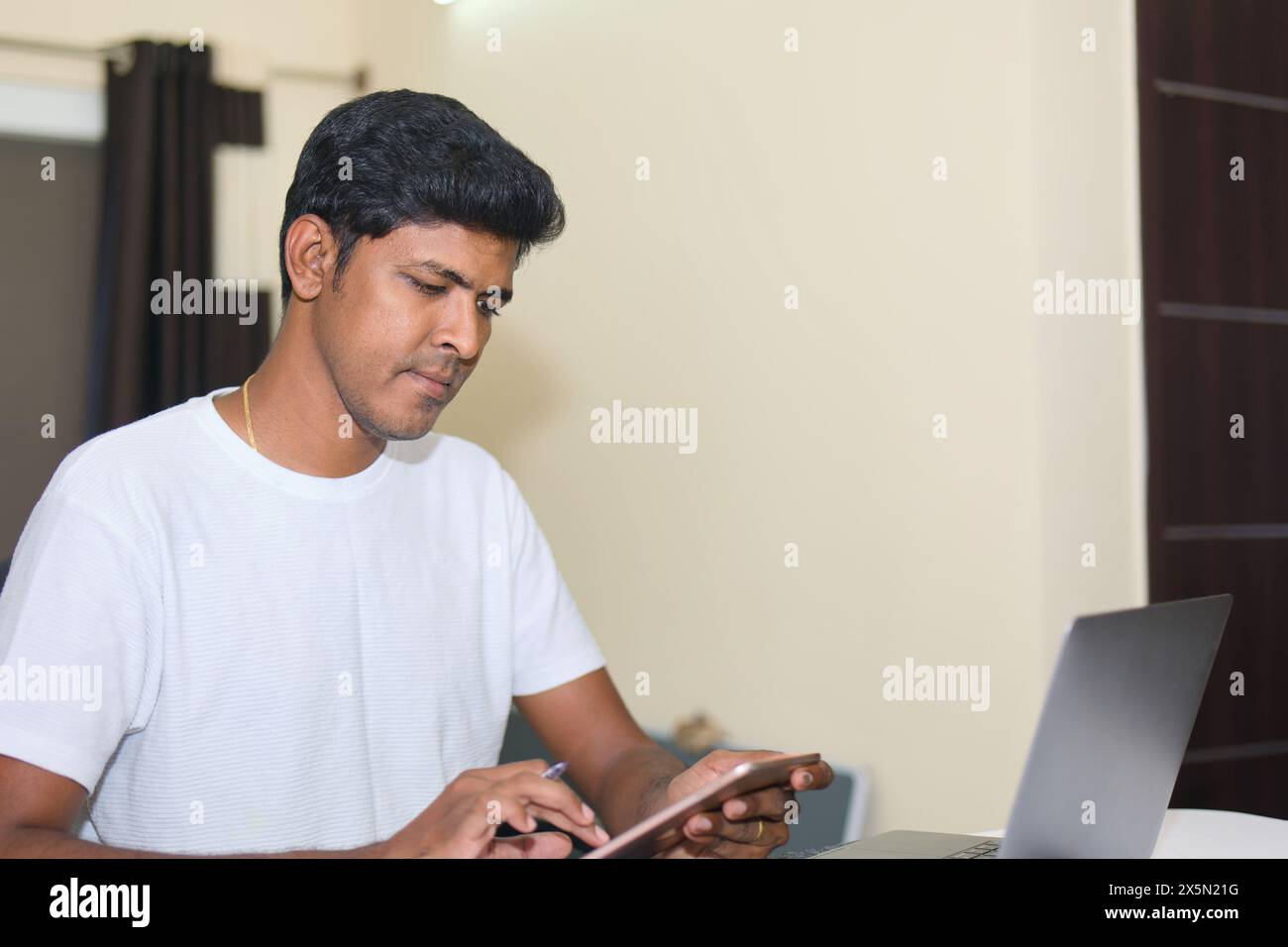 A concentrated young Indian man sits at a desk in his home office ...