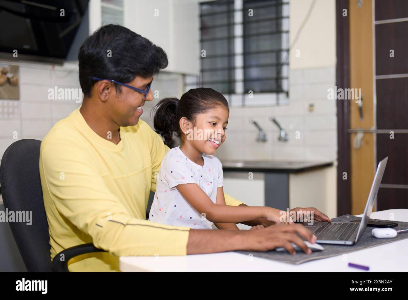 An Indian father smiles as he patiently helps his young daughter learn ...