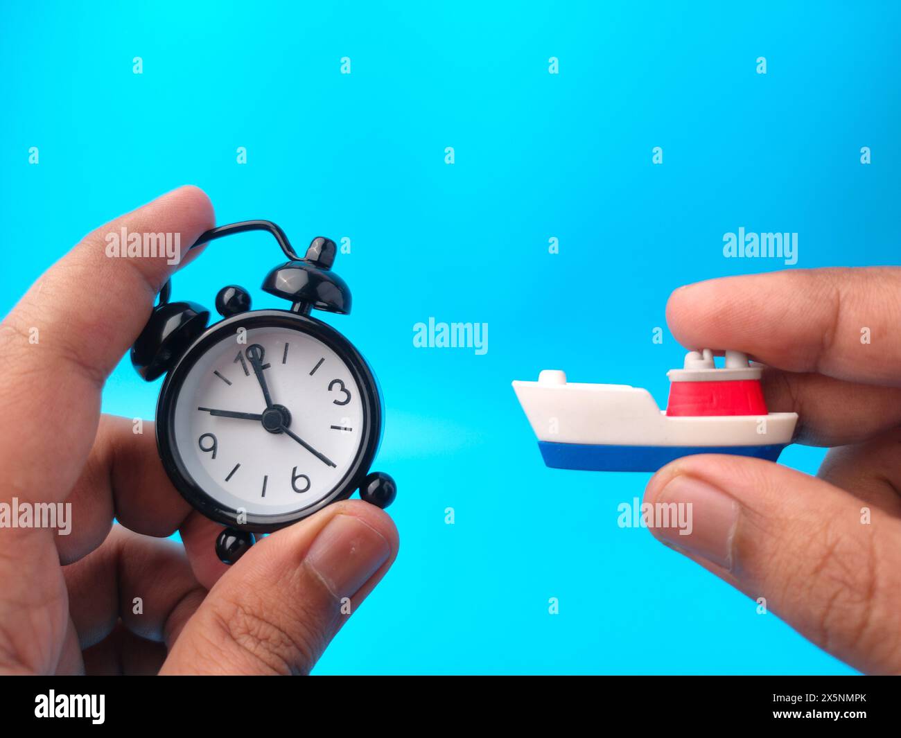 Hand holding clock and toy ships on blue background. Travel concept ...