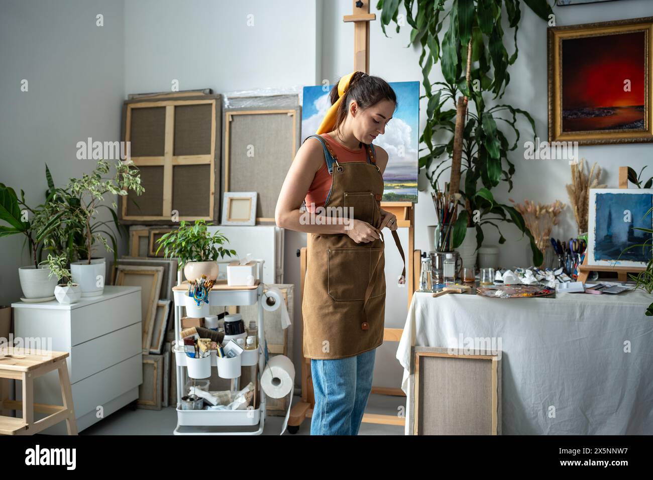 Cheerful woman painter tying apron getting ready for creative work ...