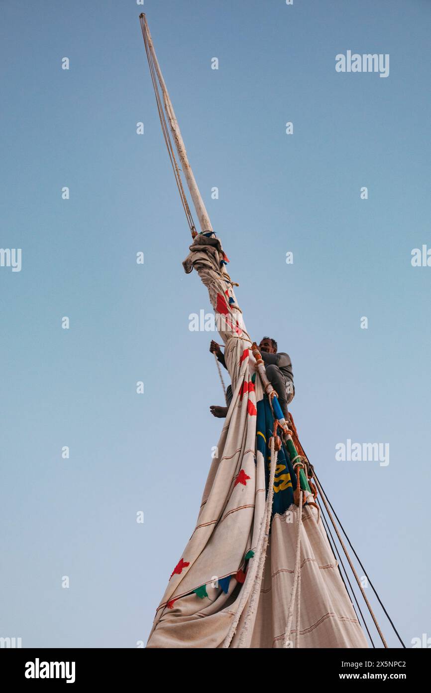 a sailor climbs up the wooden mast of his sailboat to fold up and stow ...