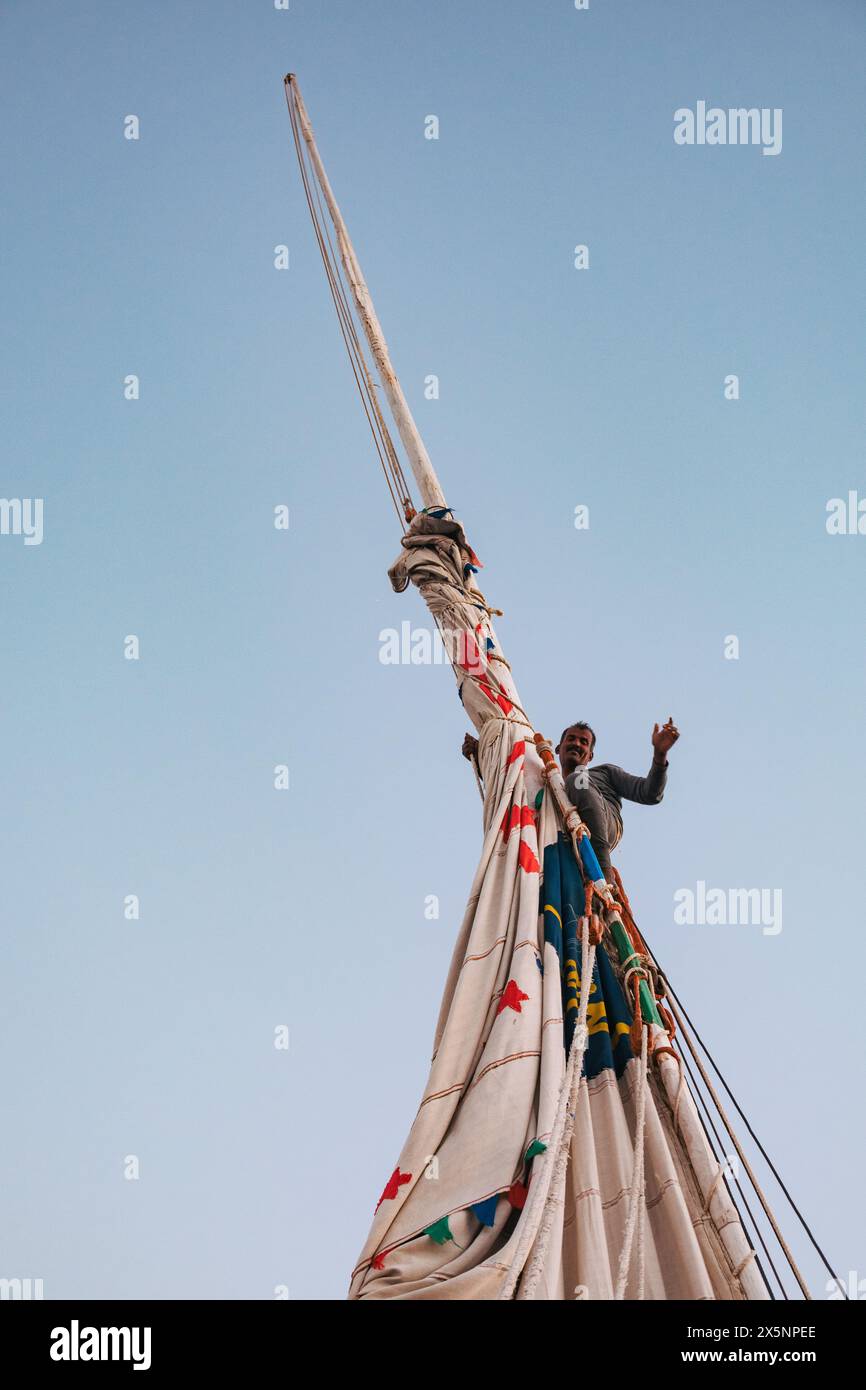 a sailor climbs up the wooden mast of his sailboat to fold up and stow ...