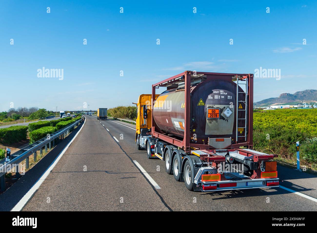 Truck driving on a highway with a tank container with labels and danger ...