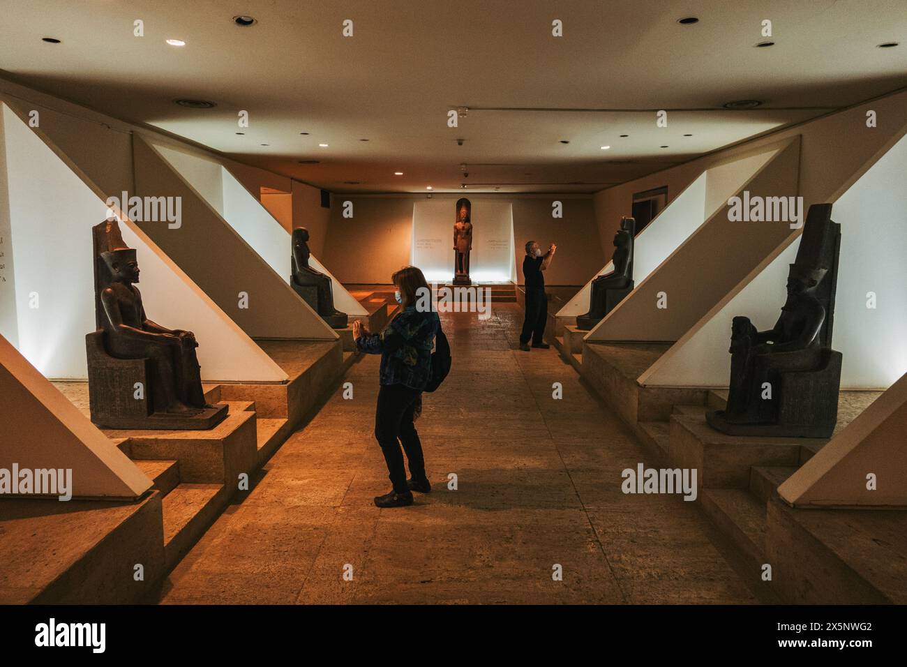 Visitors explore a dimly lit gallery of seated pharaoh statues at the ...