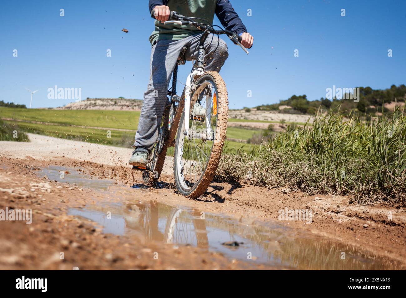 A boy rides his bicycle on a muddy road splashing mud as he passes ...