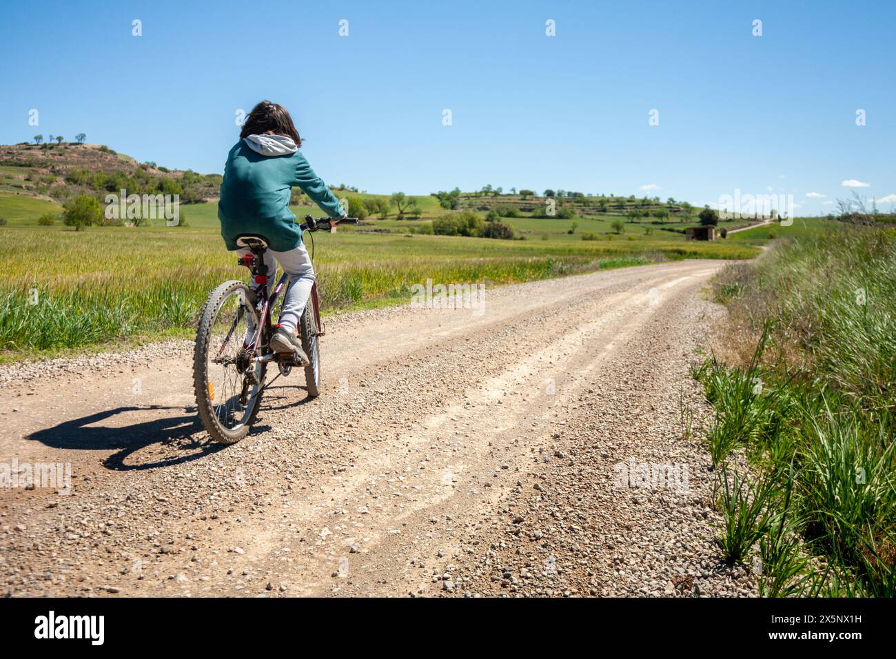 A young boy is riding a bike down a dirt road. The road is bumpy and ...