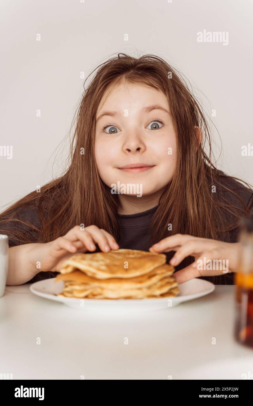 Little cheerful teenage girl getting ready to eat a stack of pancakes ...