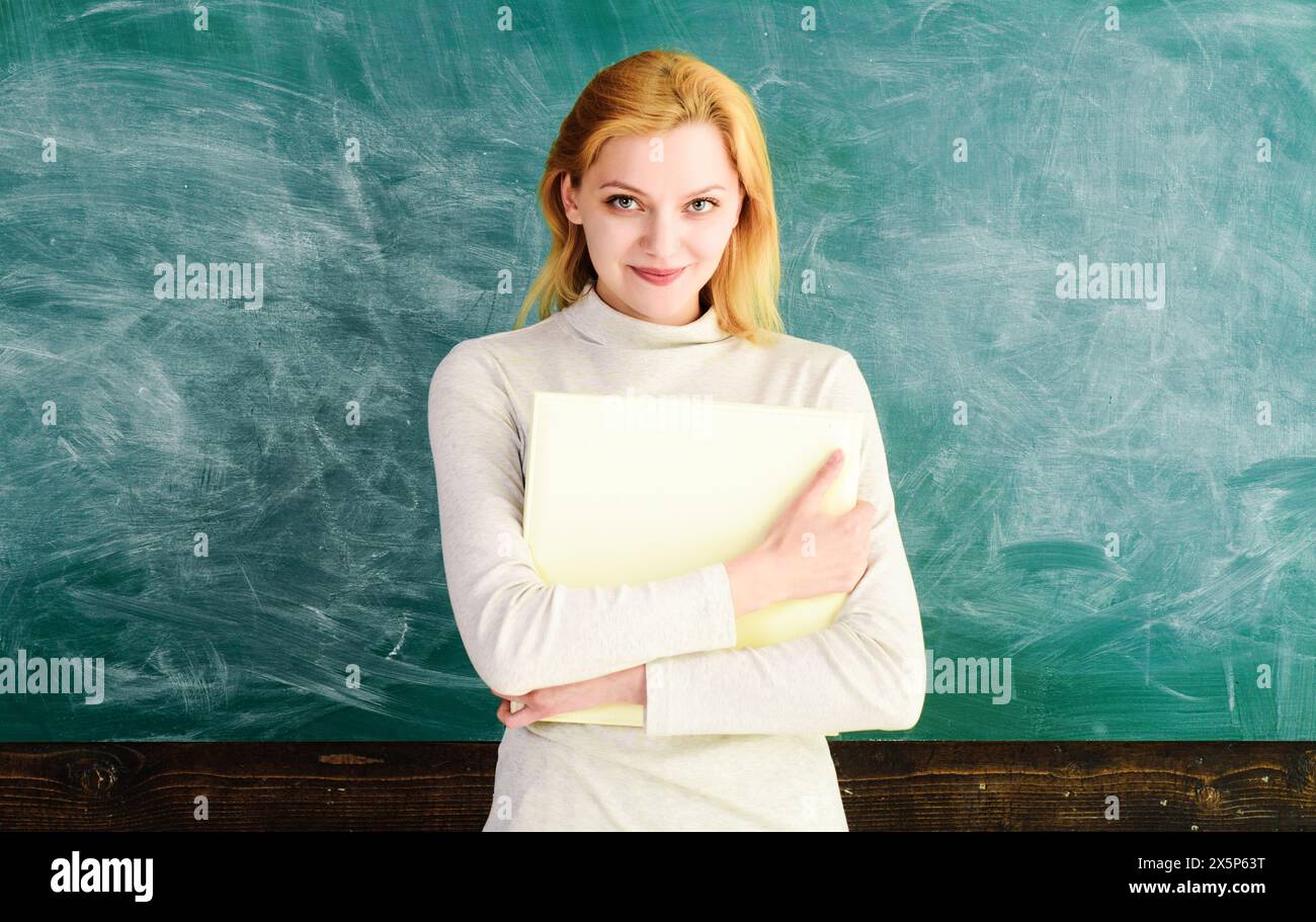 Smiling female teacher standing with teacher's journal in front of ...
