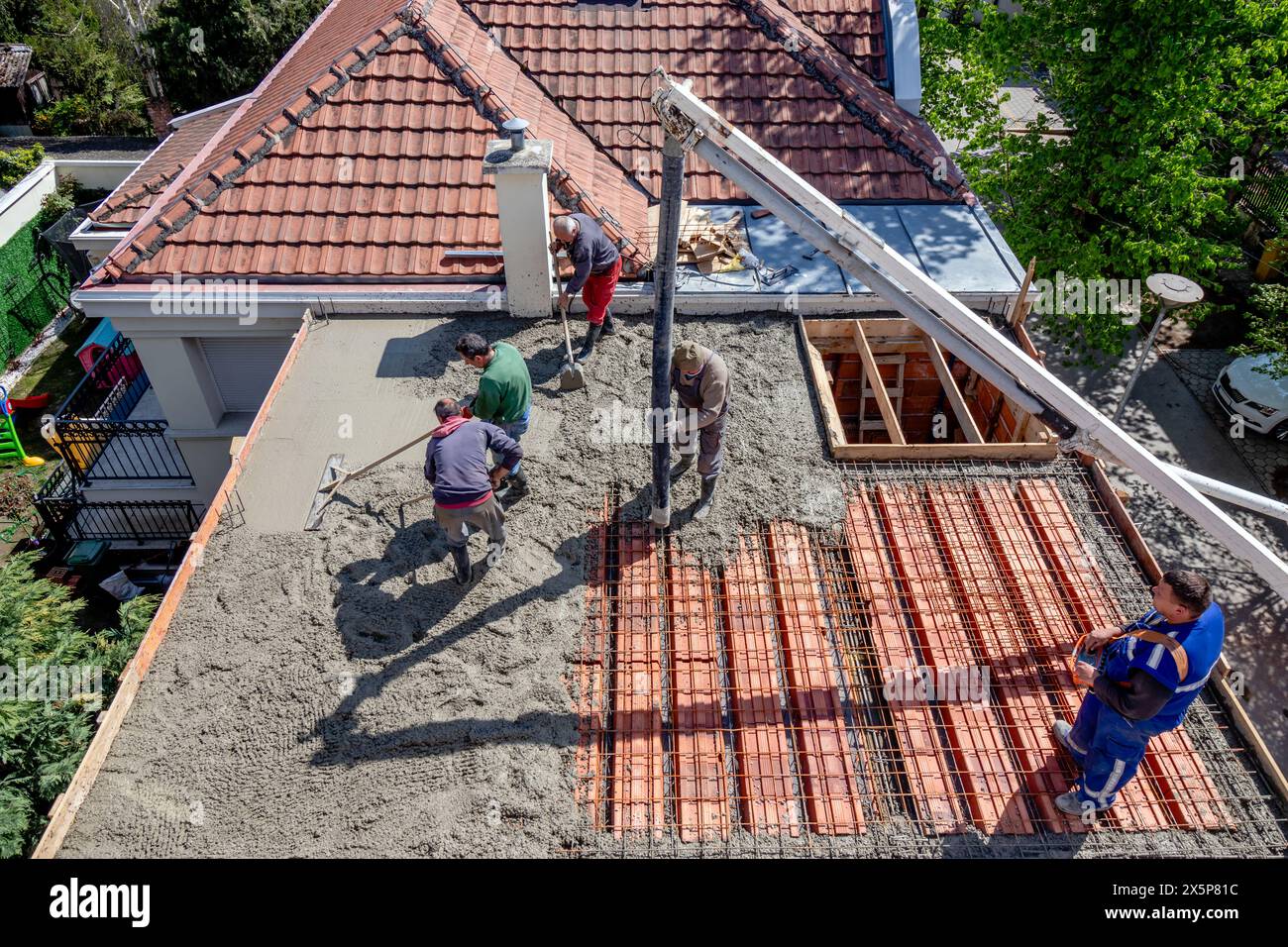 Construction workers pour concrete mix on a steel reinforced roof slab ...
