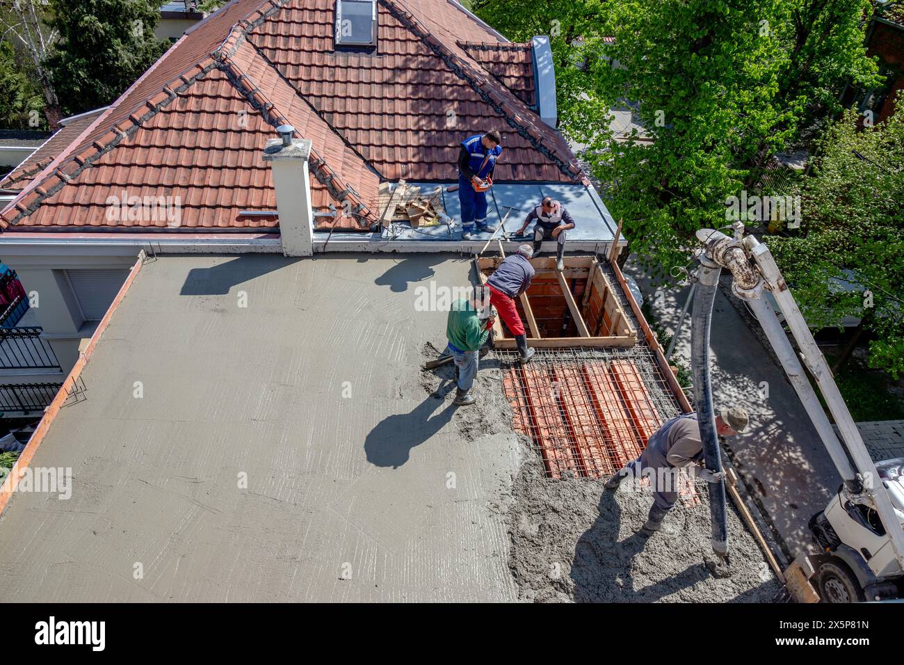Construction workers pour concrete mix on a steel reinforced roof slab ...