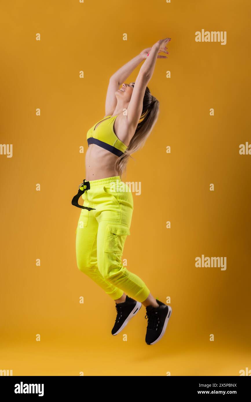 Beautiful happy girl in yellow outfit jumping against dark yellow or ...