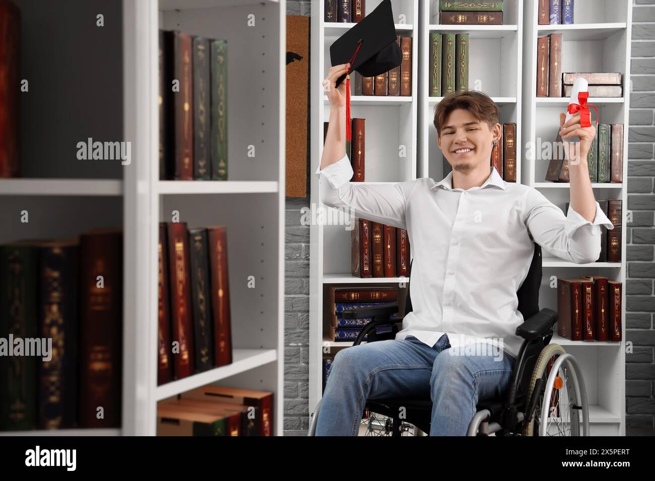Male graduate in wheelchair with diploma and hat at library Stock Photo ...