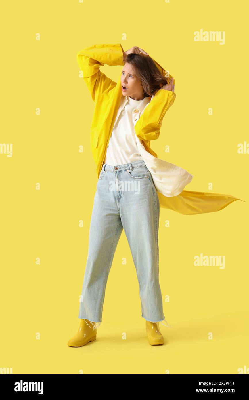Young woman in raincoat with strong wind on yellow background Stock ...