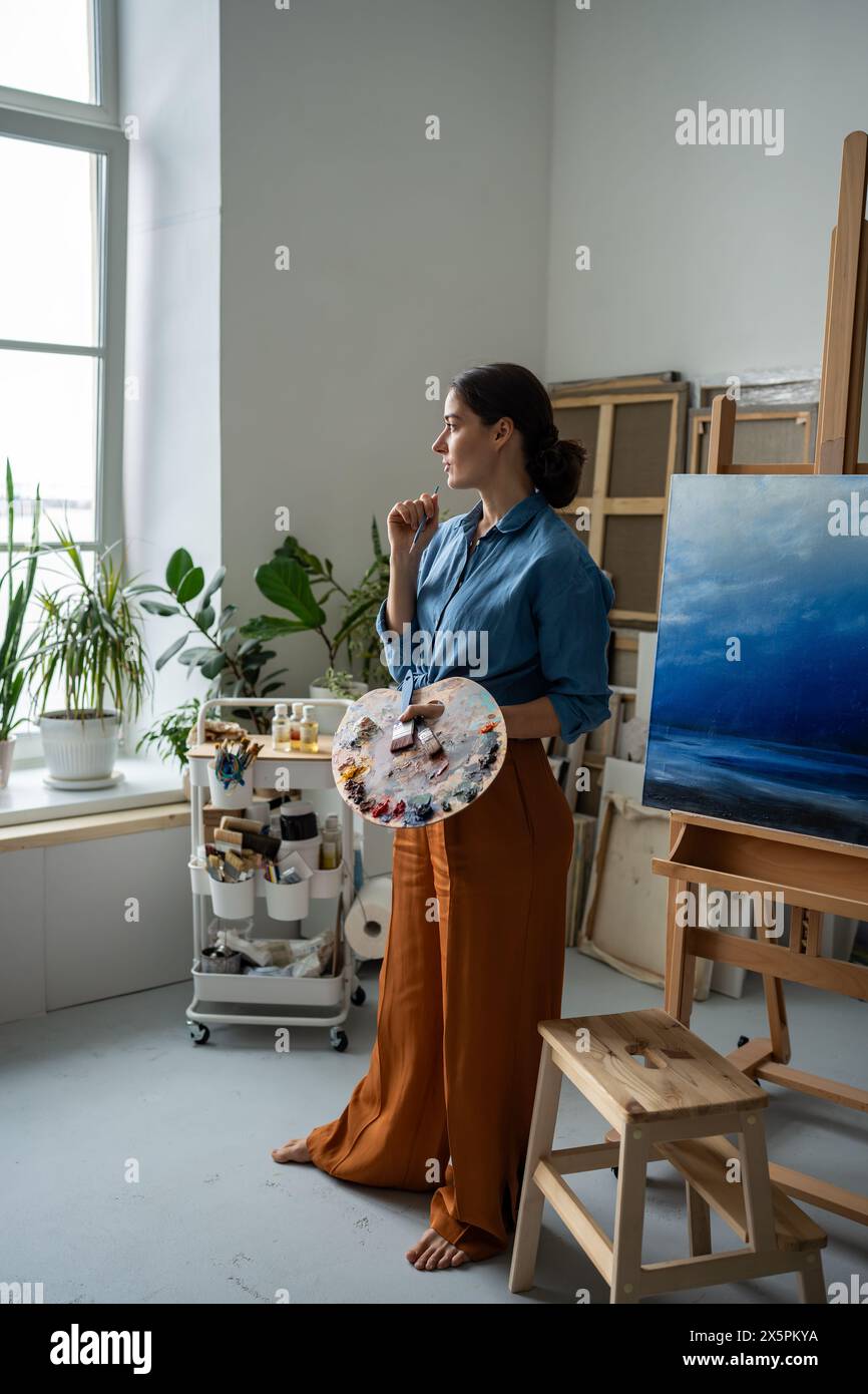 Contemplative woman artist seeking for inspiration, looks out window ...