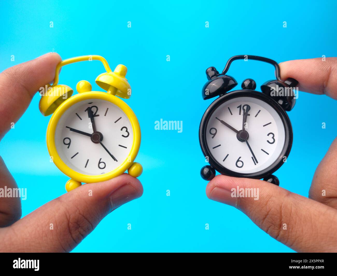 Hand holding two alarm clock on blue background Stock Photo - Alamy
