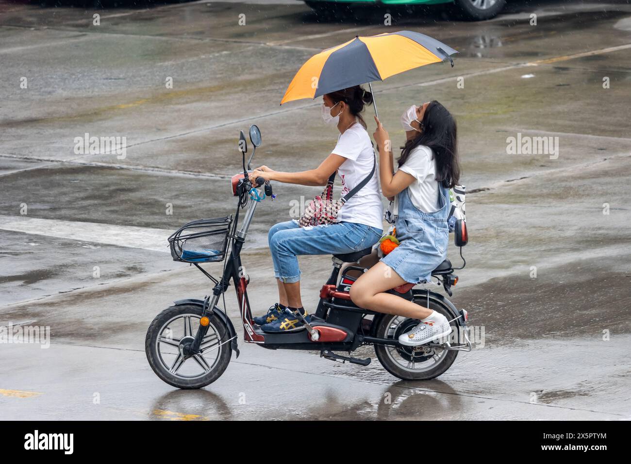 SAMUT PRAKAN, THAILAND, MAR 20 2024, Two women with umbrellas ride an ...