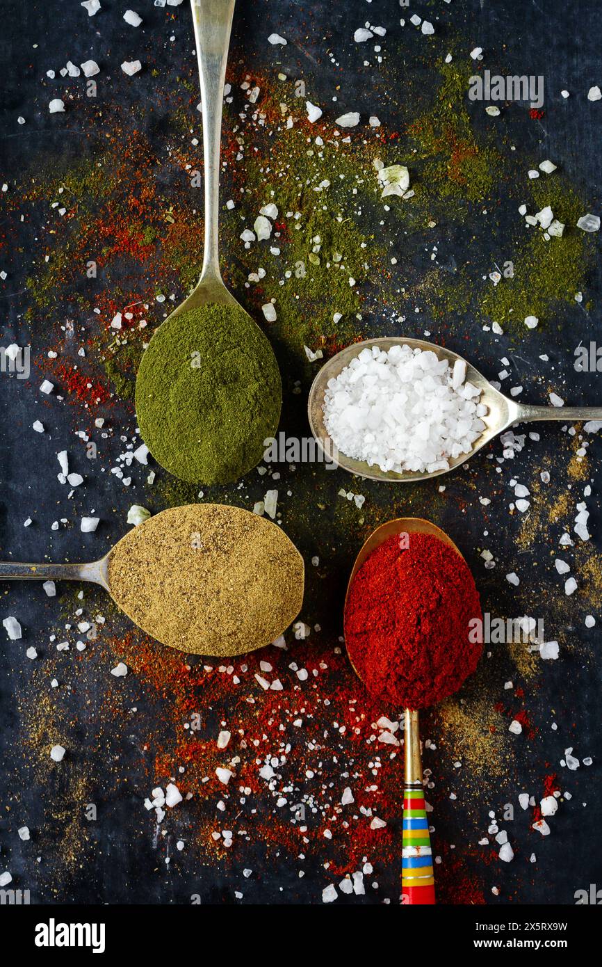 Spoons with spices and salt on black background sprinkled with ...