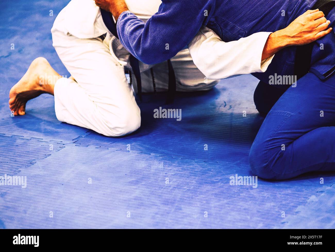 Two men on a blue mat in a Brazilian Jiu-Jitsu training facility. He is ...