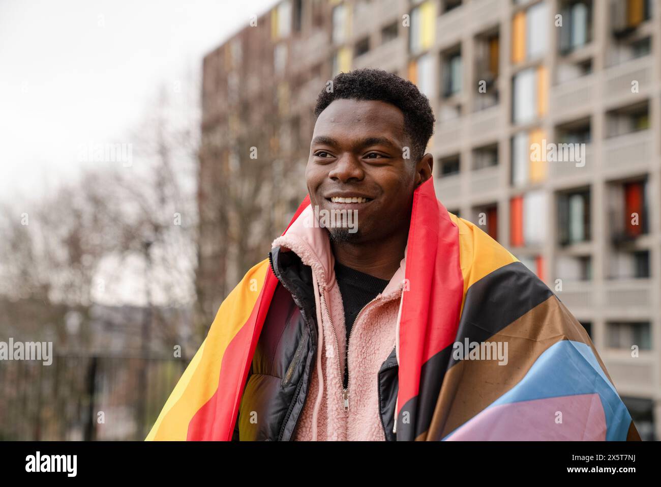 Smiling young man wrapped in progress pride flag Stock Photo - Alamy