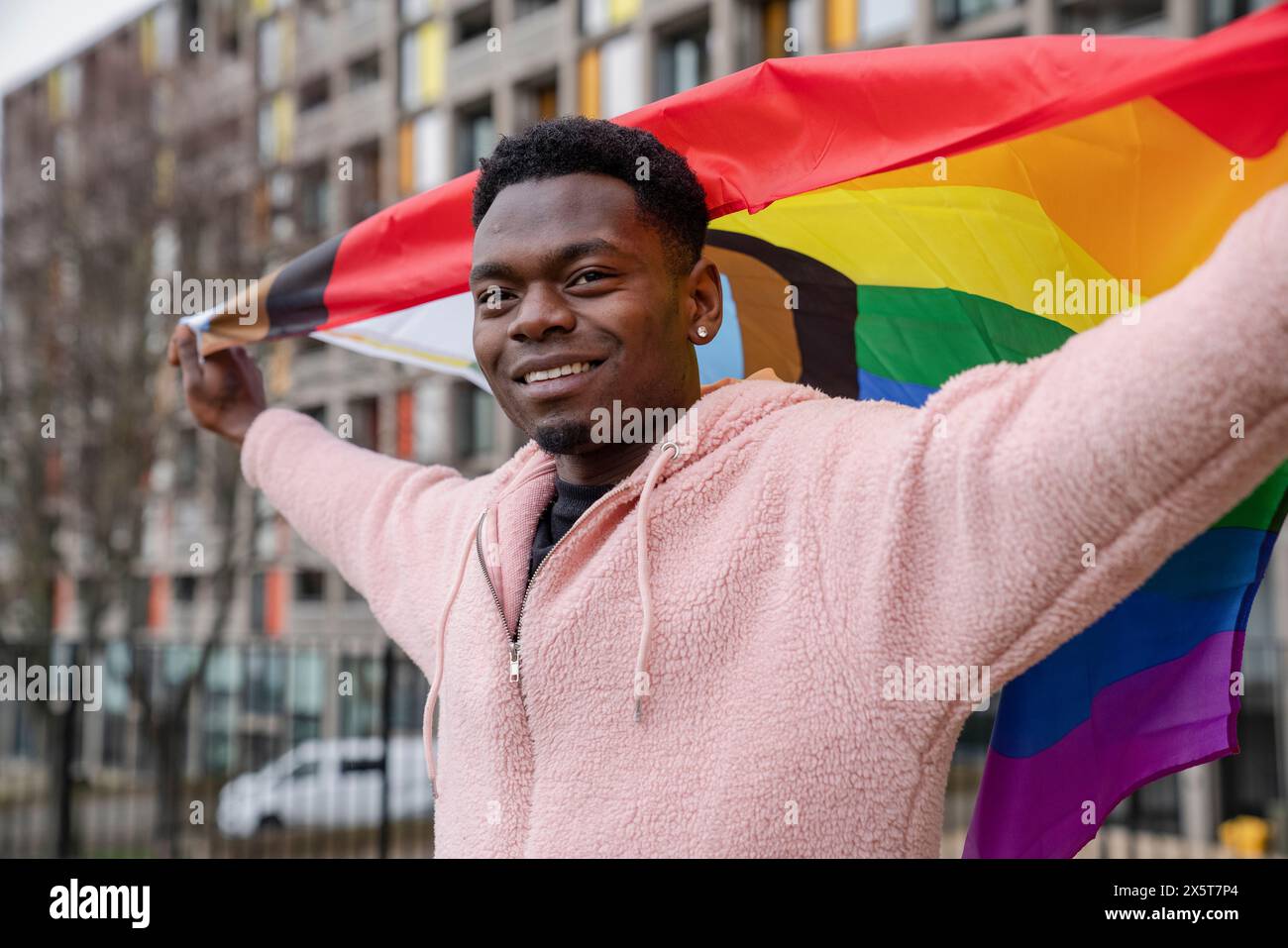Smiling young man holding progress pride flag Stock Photo - Alamy