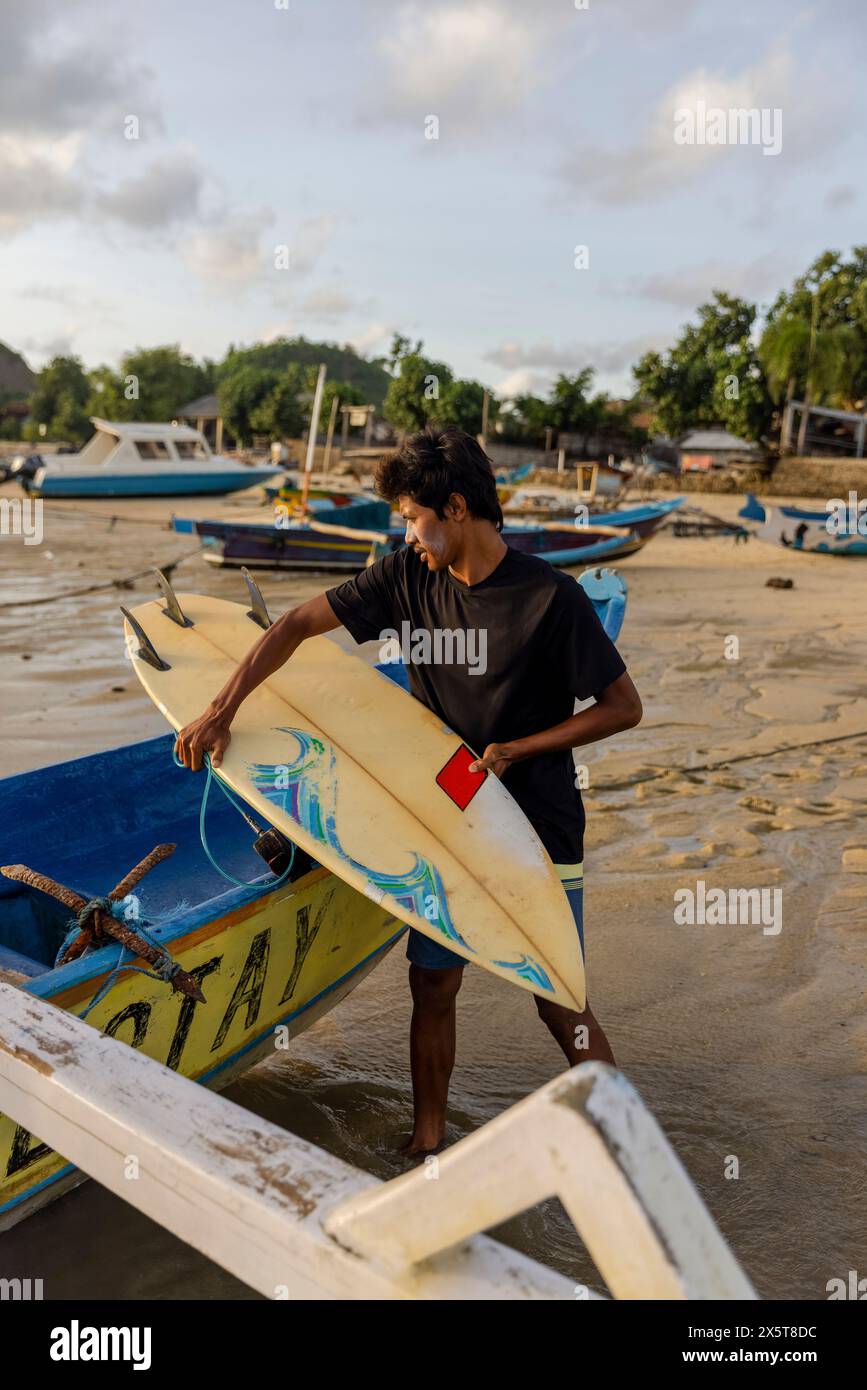 Indonesia, Lombok, Male surfer packing surfboard on boat at beach Stock ...