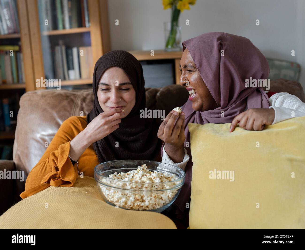 Friends sitting on sofa, laughing and eating popcorn together Stock ...