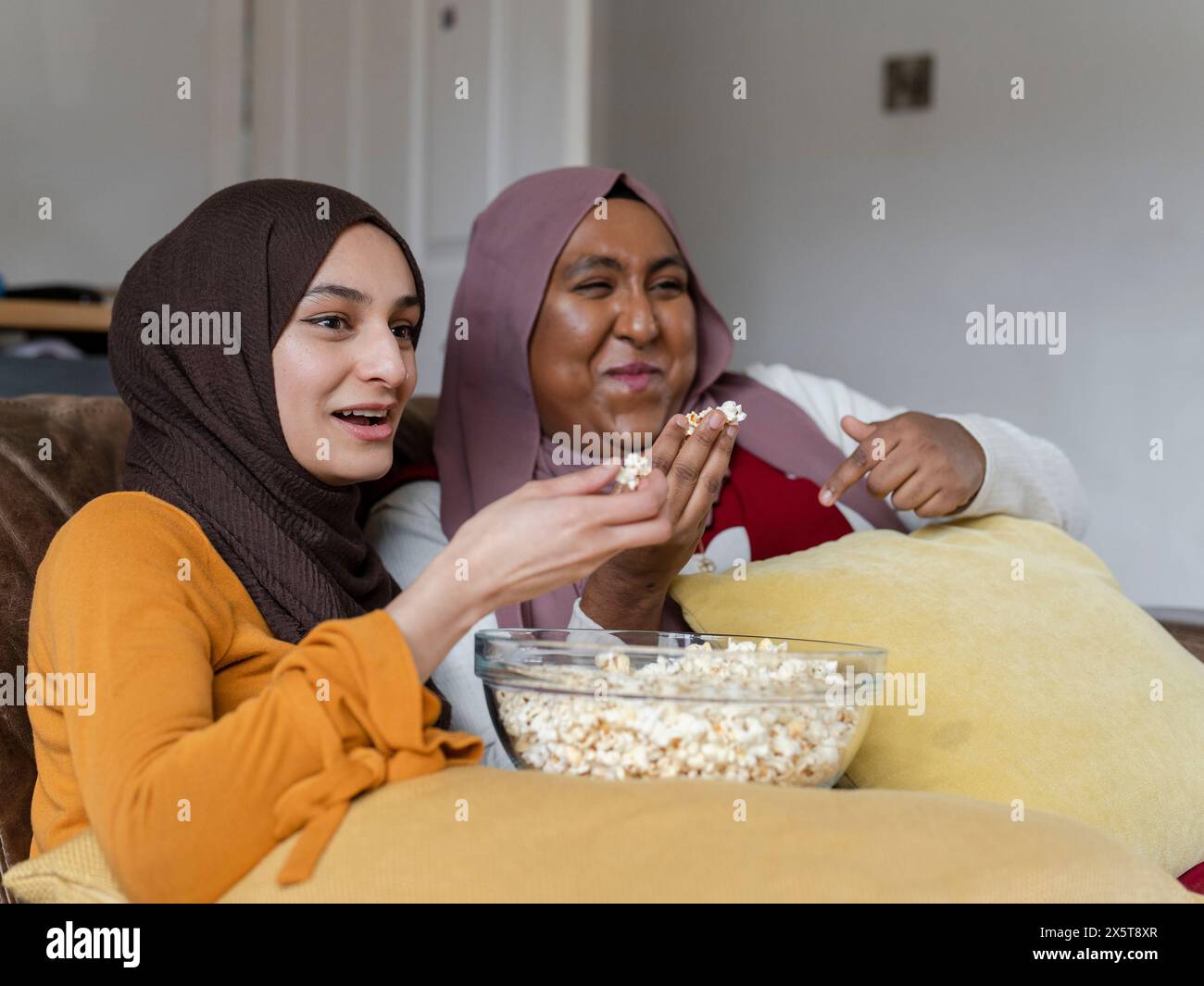 Cheerful friends eating popcorn while watching TV at home Stock Photo ...