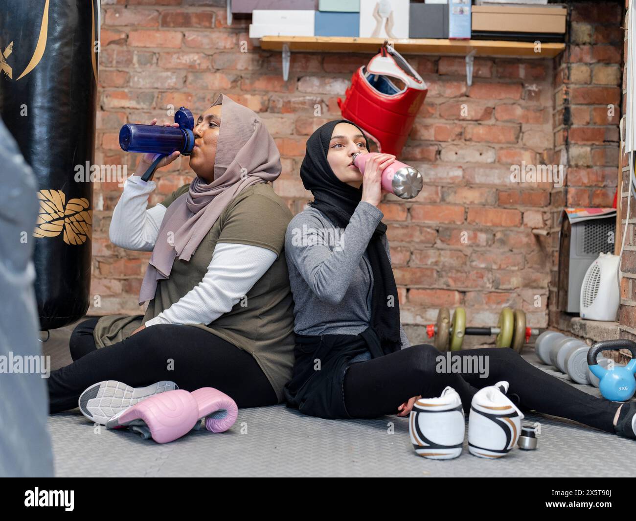 Two women sitting in gym, resting and drinking water Stock Photo - Alamy
