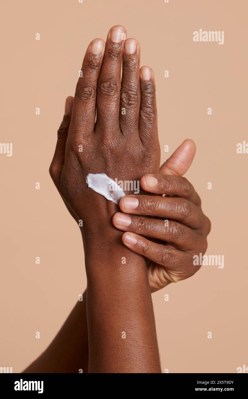 Woman applying hand cream against beige background Stock Photo - Alamy