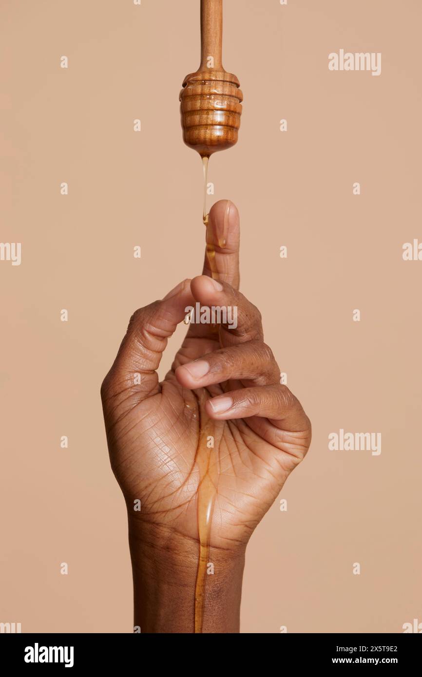 Honey falling of honey dipper on woman hand against beige background ...