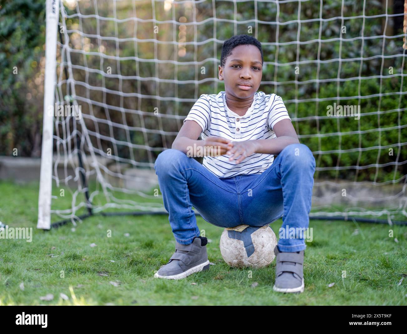 Portrait of boy (8-9) sitting on football in back yard Stock Photo - Alamy