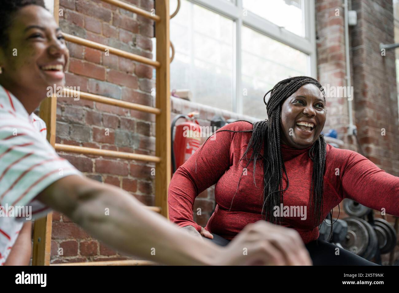 Mother and daughter laughing while doing stretching exercises in gym ...