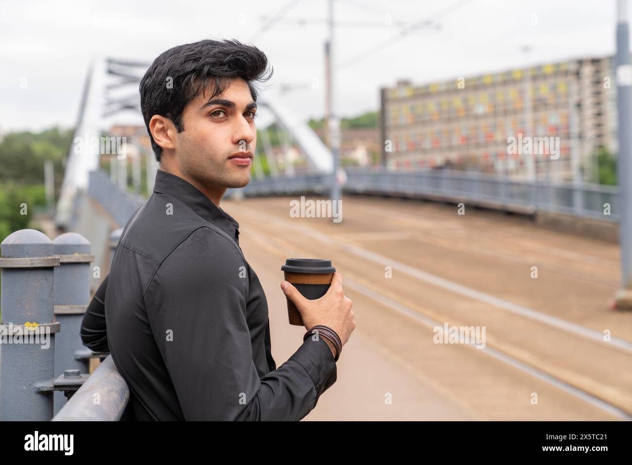 Young man leaning on railing with disposable cup Stock Photo - Alamy