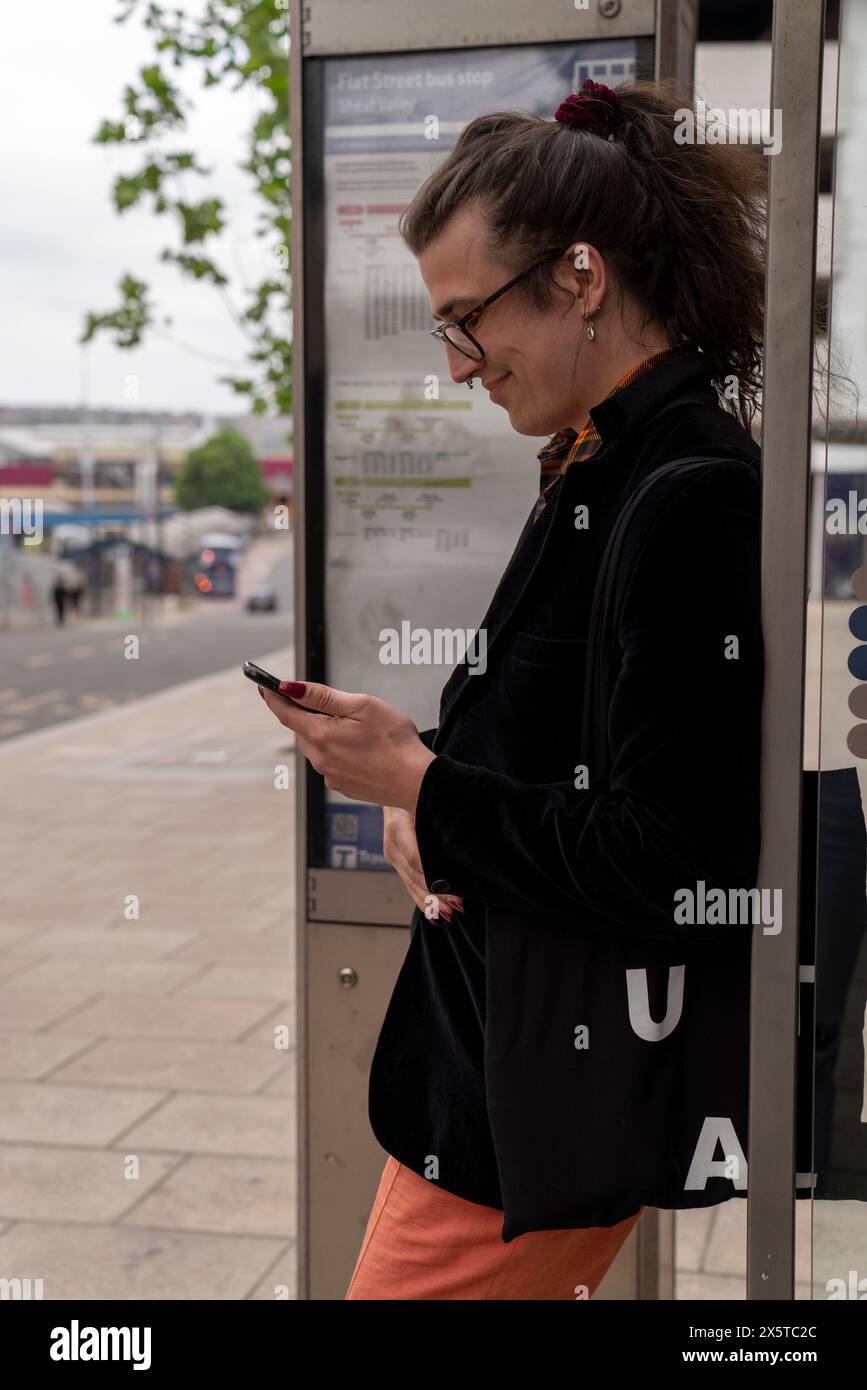 Young man using phone while waiting at bus stop Stock Photo - Alamy