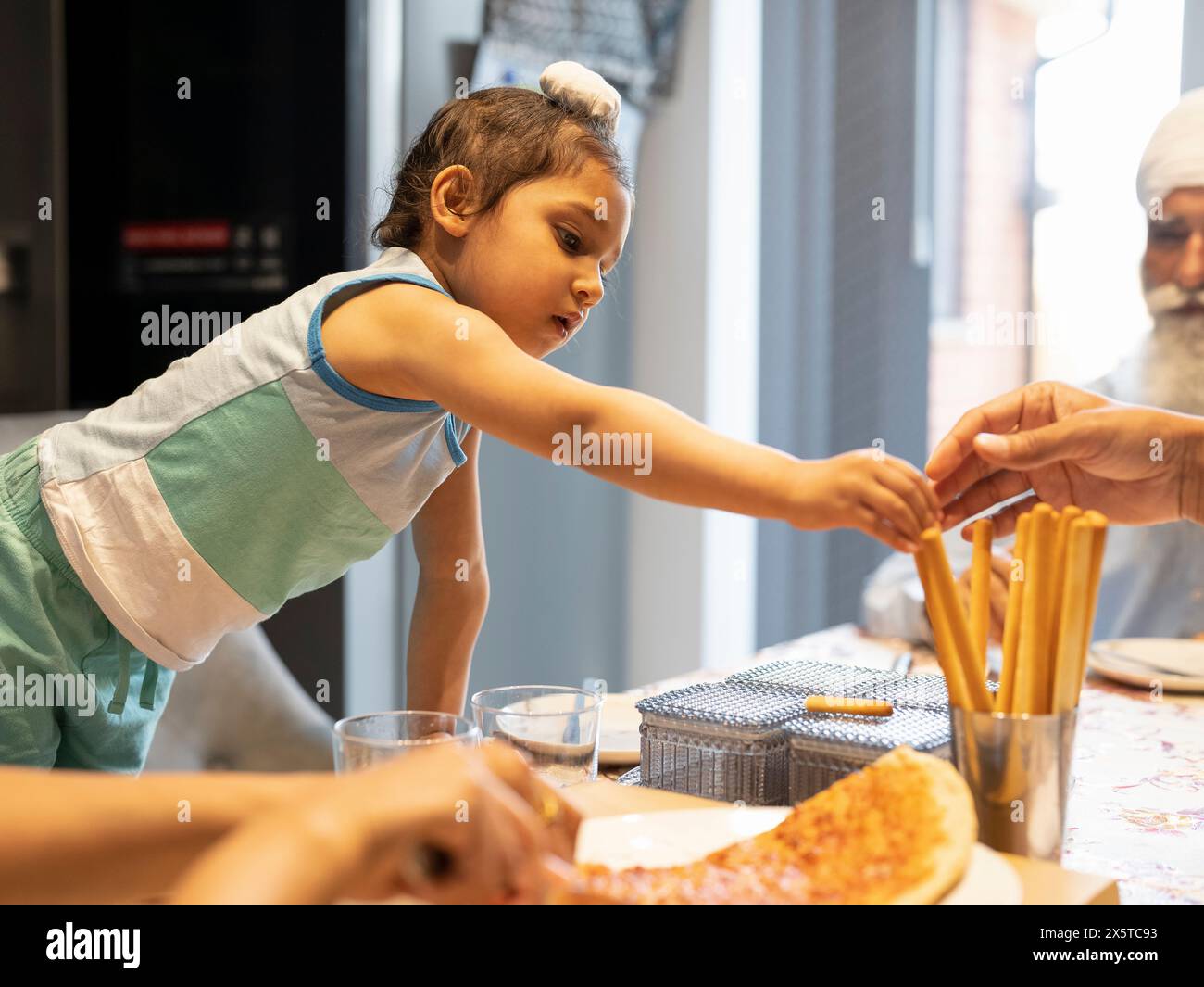 Boy (2-3) reaching for breadsticks during dinner with family Stock ...