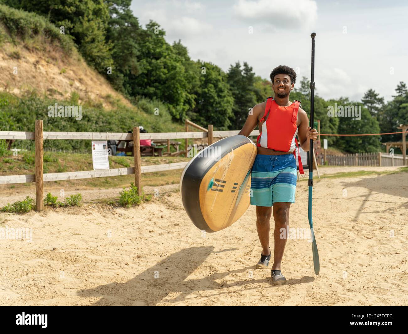 Young man carrying paddleboard and oar on beach Stock Photo - Alamy