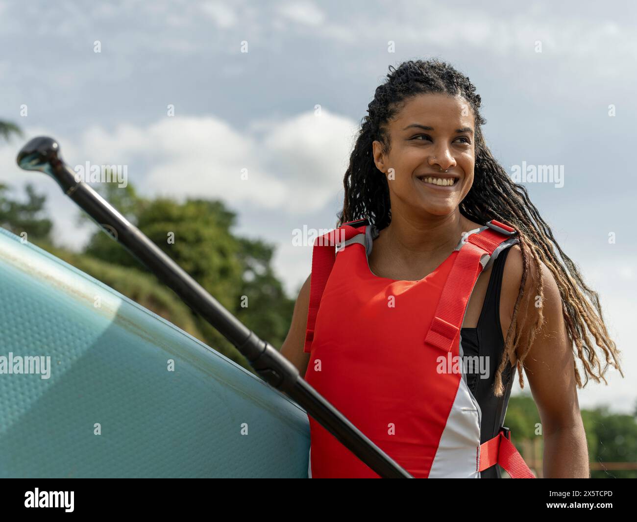 Portrait of smiling woman carrying paddleboard and oar Stock Photo - Alamy