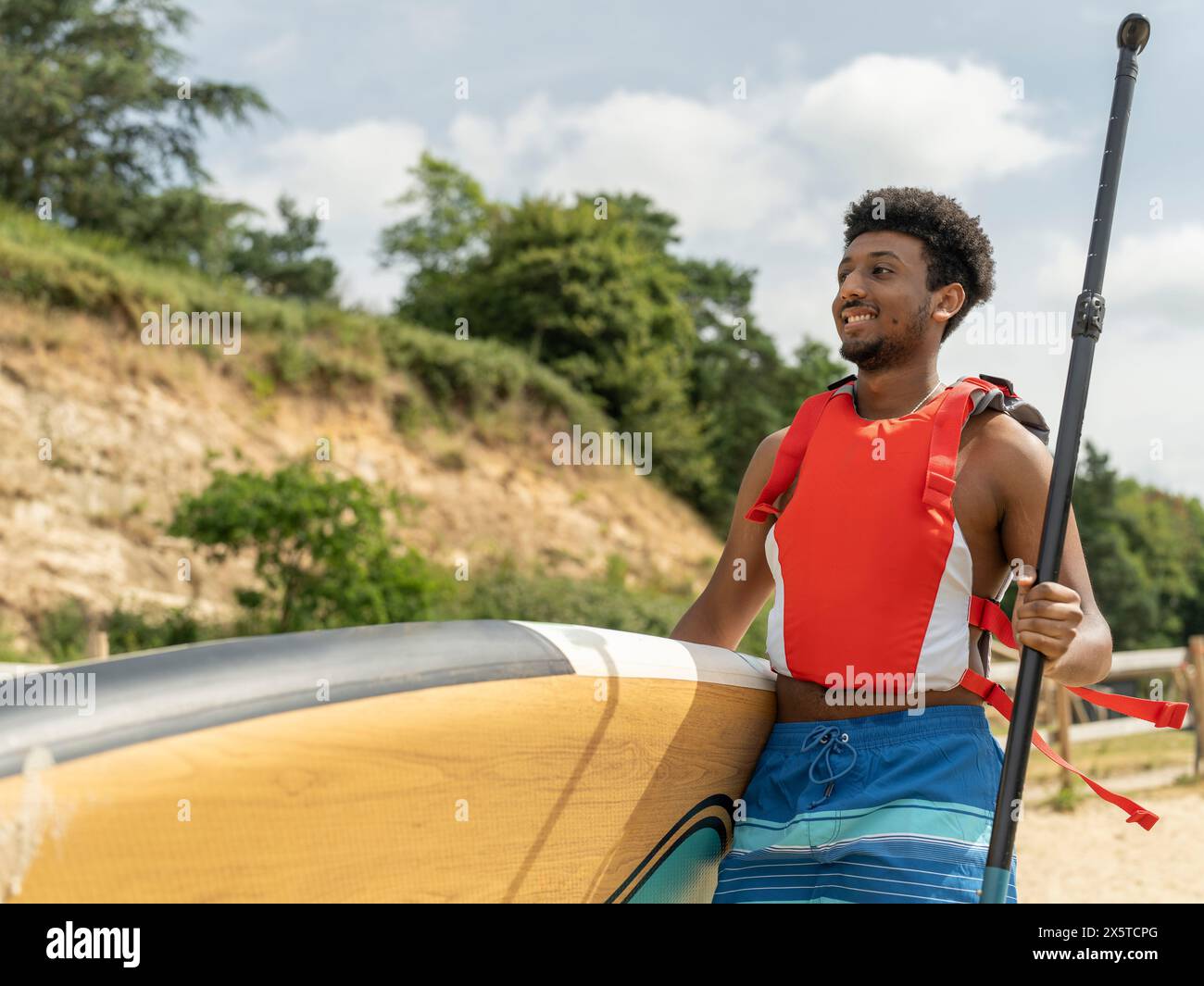 Young man carrying paddleboard and oar on beach Stock Photo - Alamy