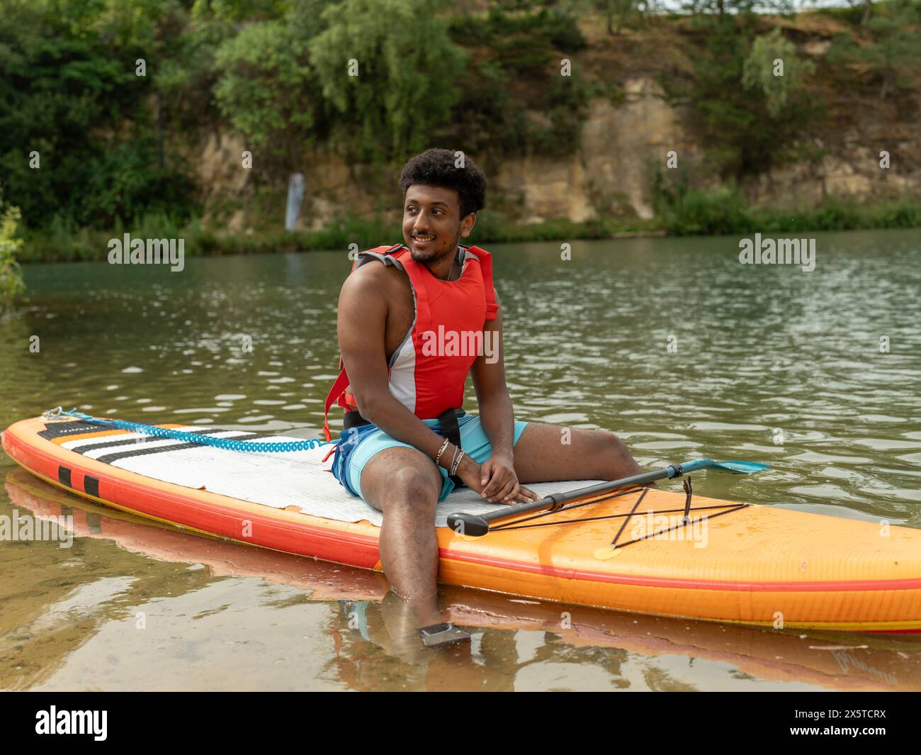Young man sitting on paddleboard on lake Stock Photo - Alamy