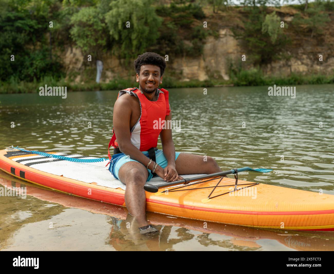 Portrait of young man sitting on paddleboard on lake Stock Photo - Alamy