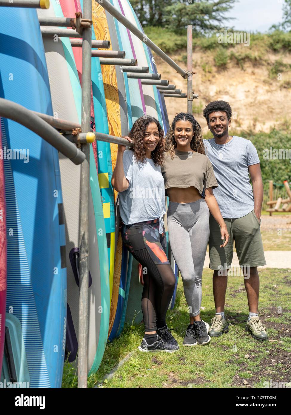 Portrait of smiling friends standing next to paddleboard rack Stock ...