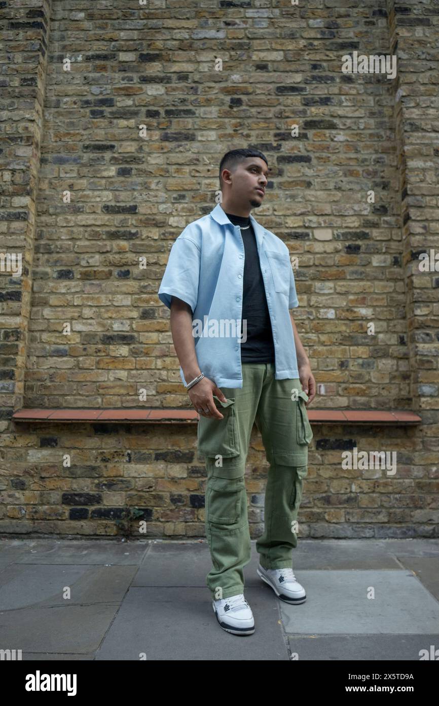Man wearing unbuttoned shirt and cargo pants standing in front of brick ...